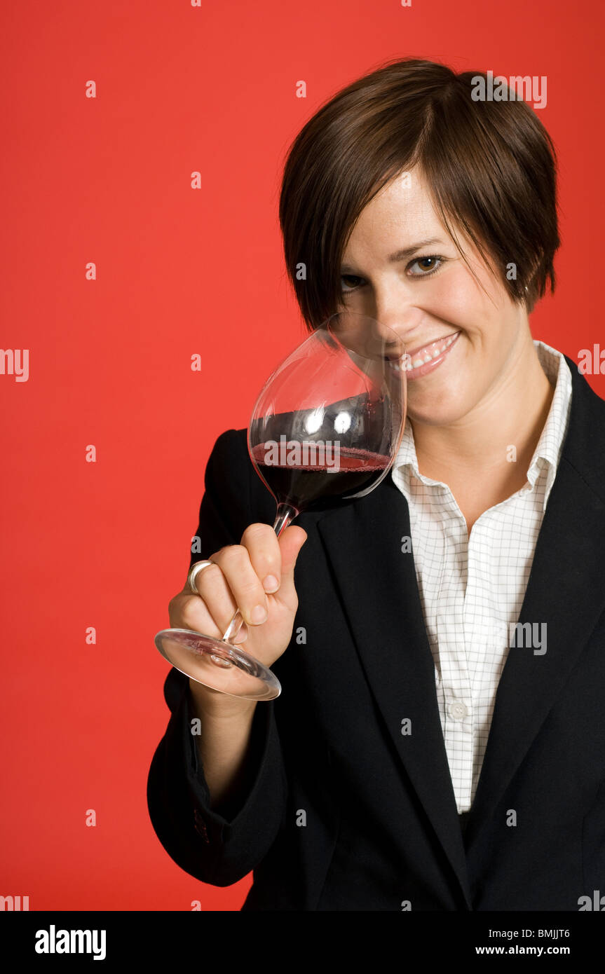 Female sommelier tasting wine against red background, smiling, portrait ...