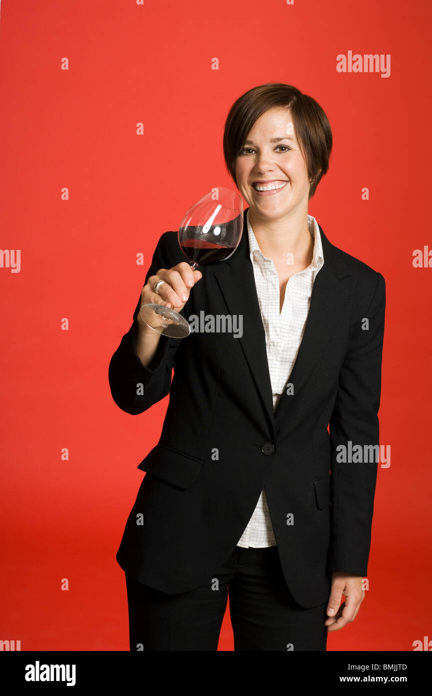 Female sommelier tasting wine against red background, smiling, portrait ...