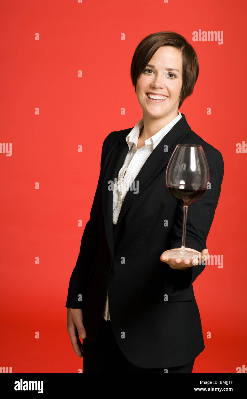 Female sommelier holding wine glass against red background, smiling ...