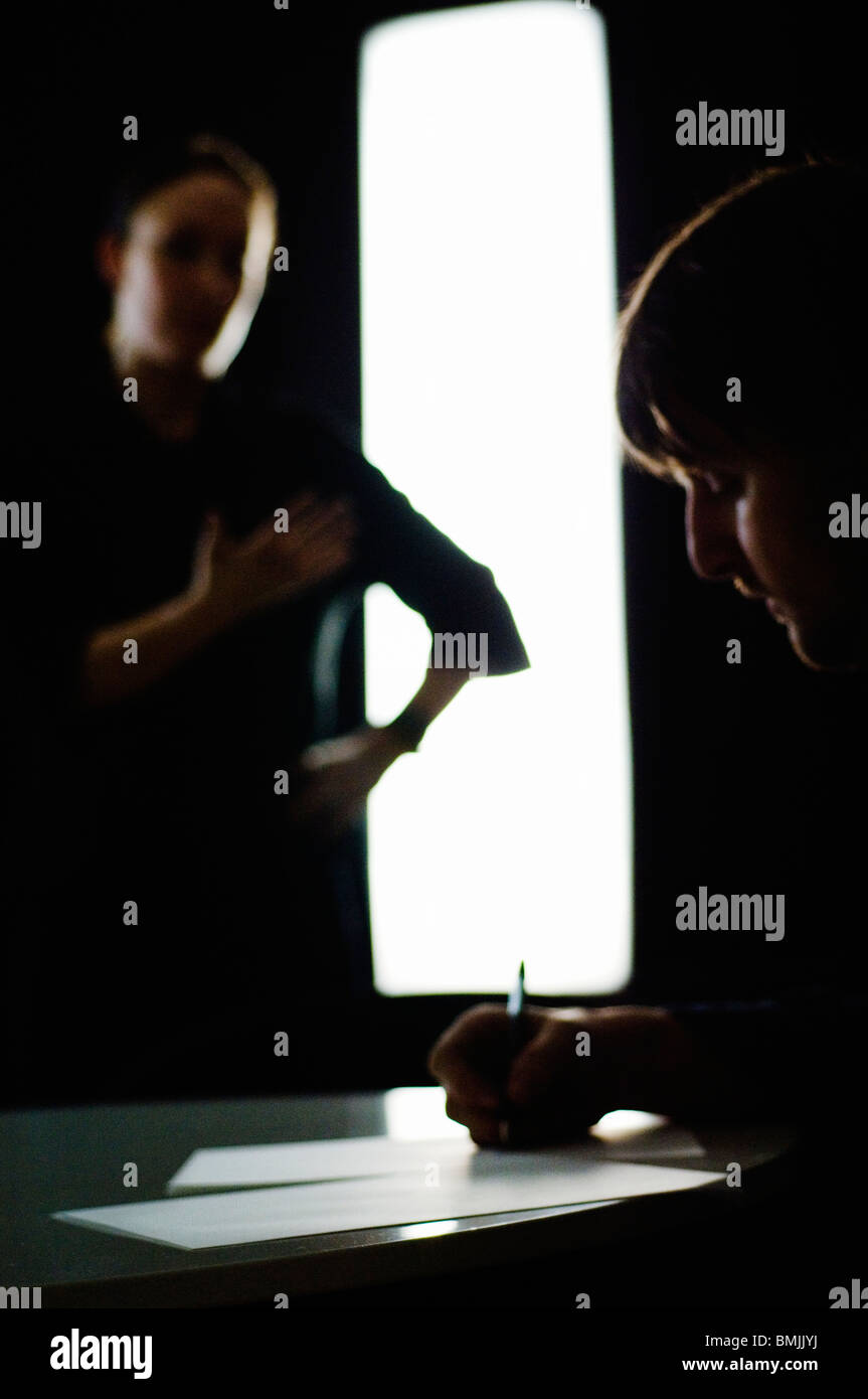 Man and woman silhouetted. Woman standing. Man seated, writing on paper ...