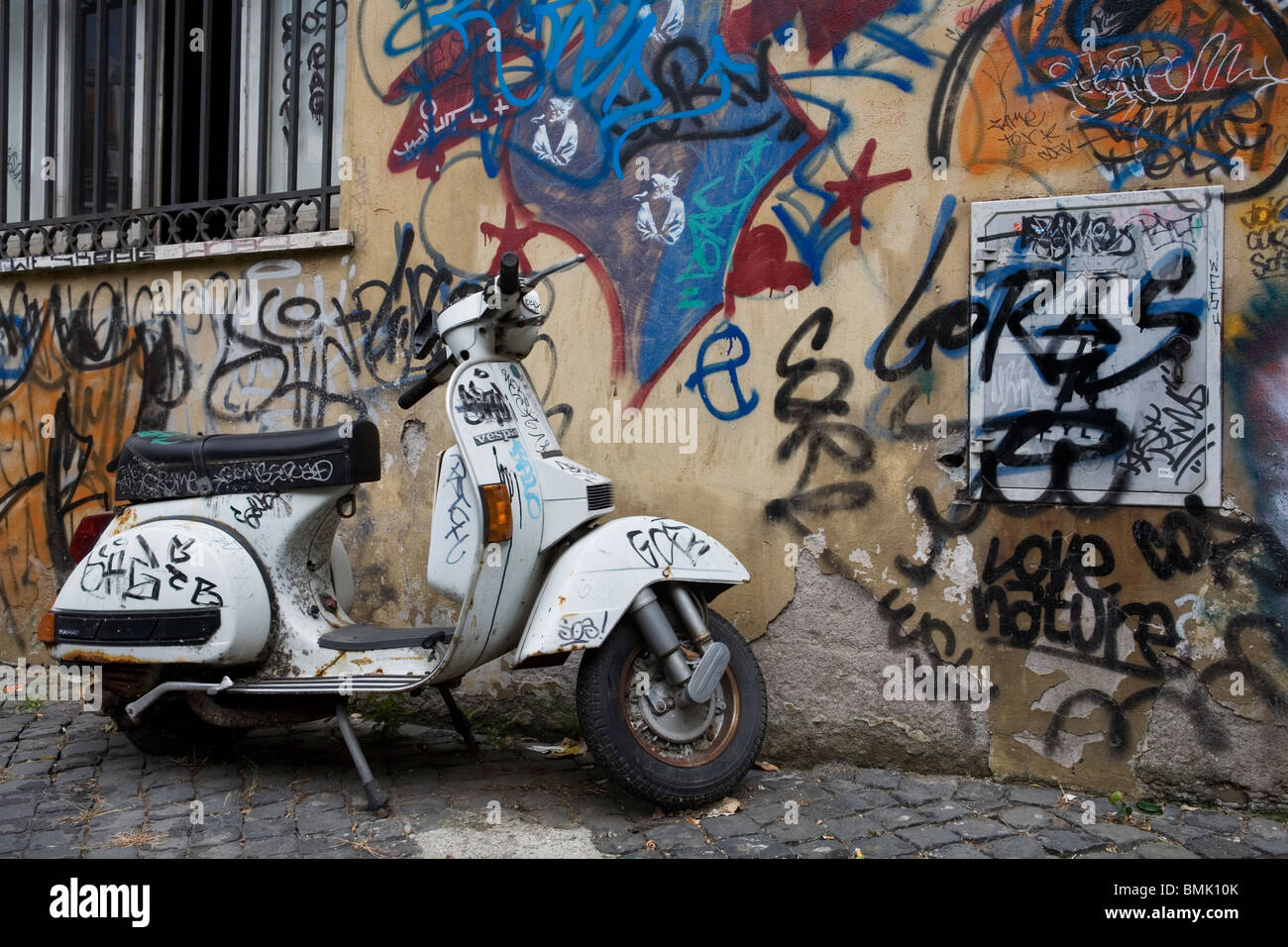 A Vespa scooter completely covered with Graffitti, in front of a wall ...