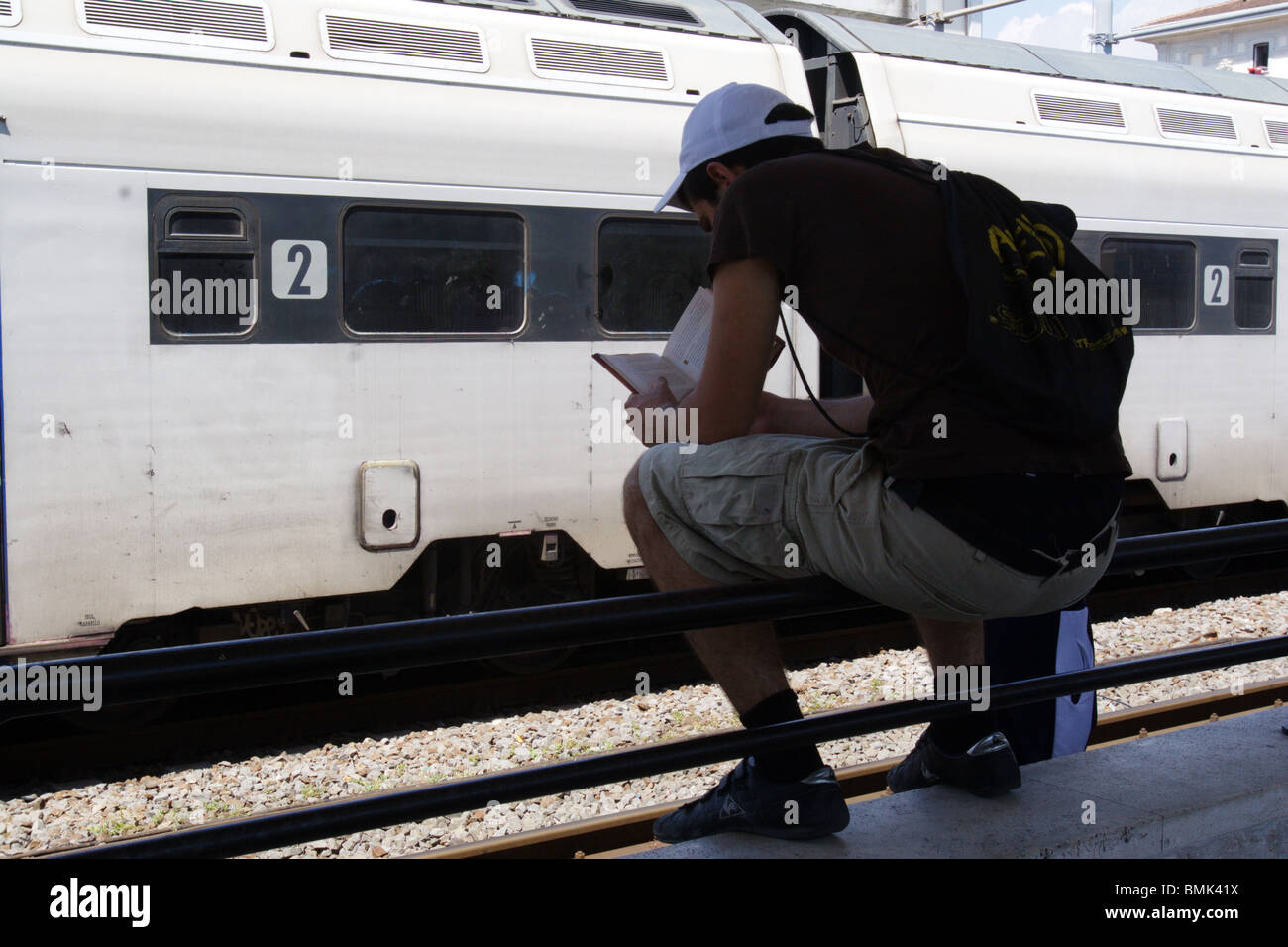 a boy read a book waiting a train in railway station. scene outdoor ...