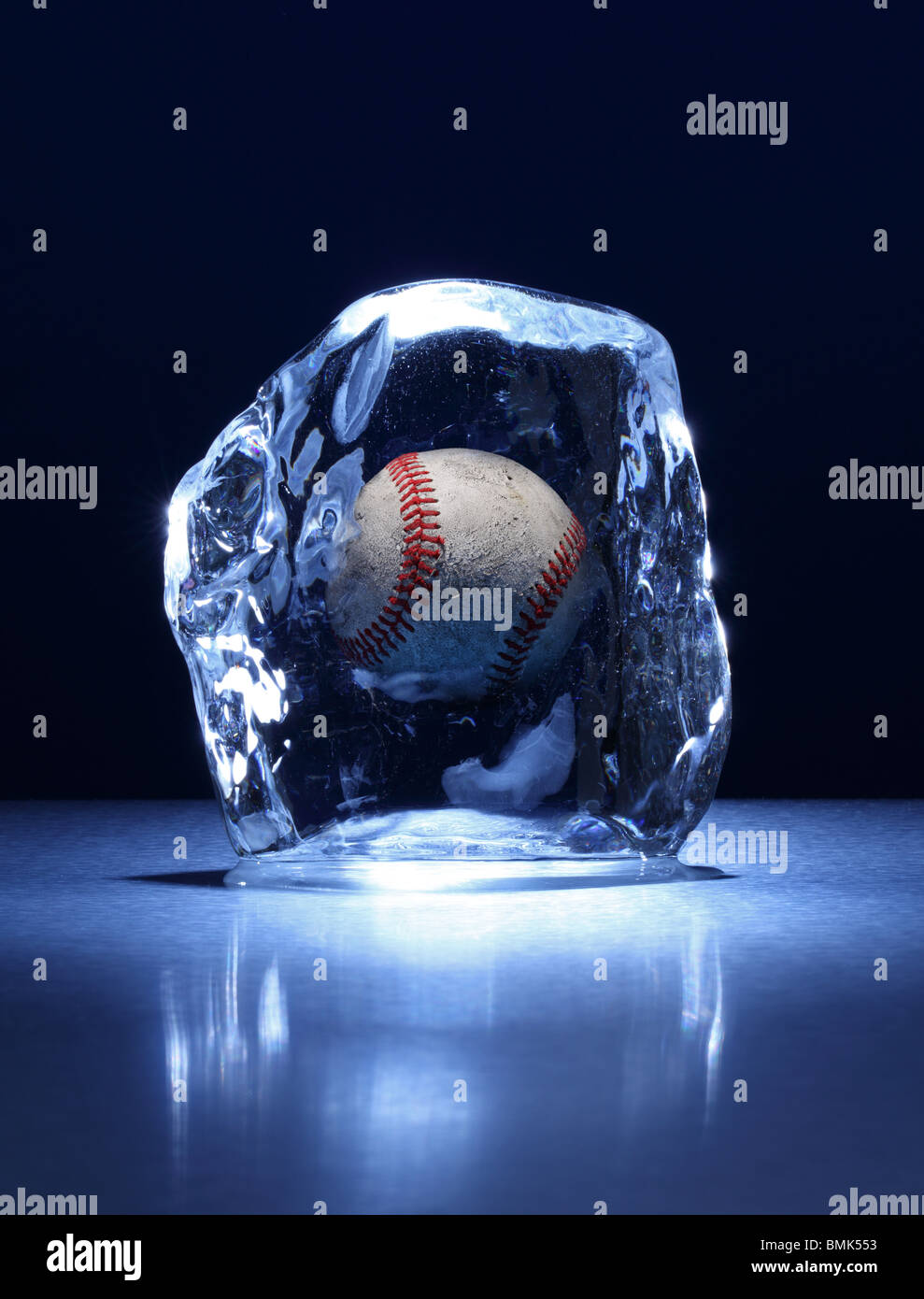 A frozen block of ice with a baseball frozen inside on a metal surface ...