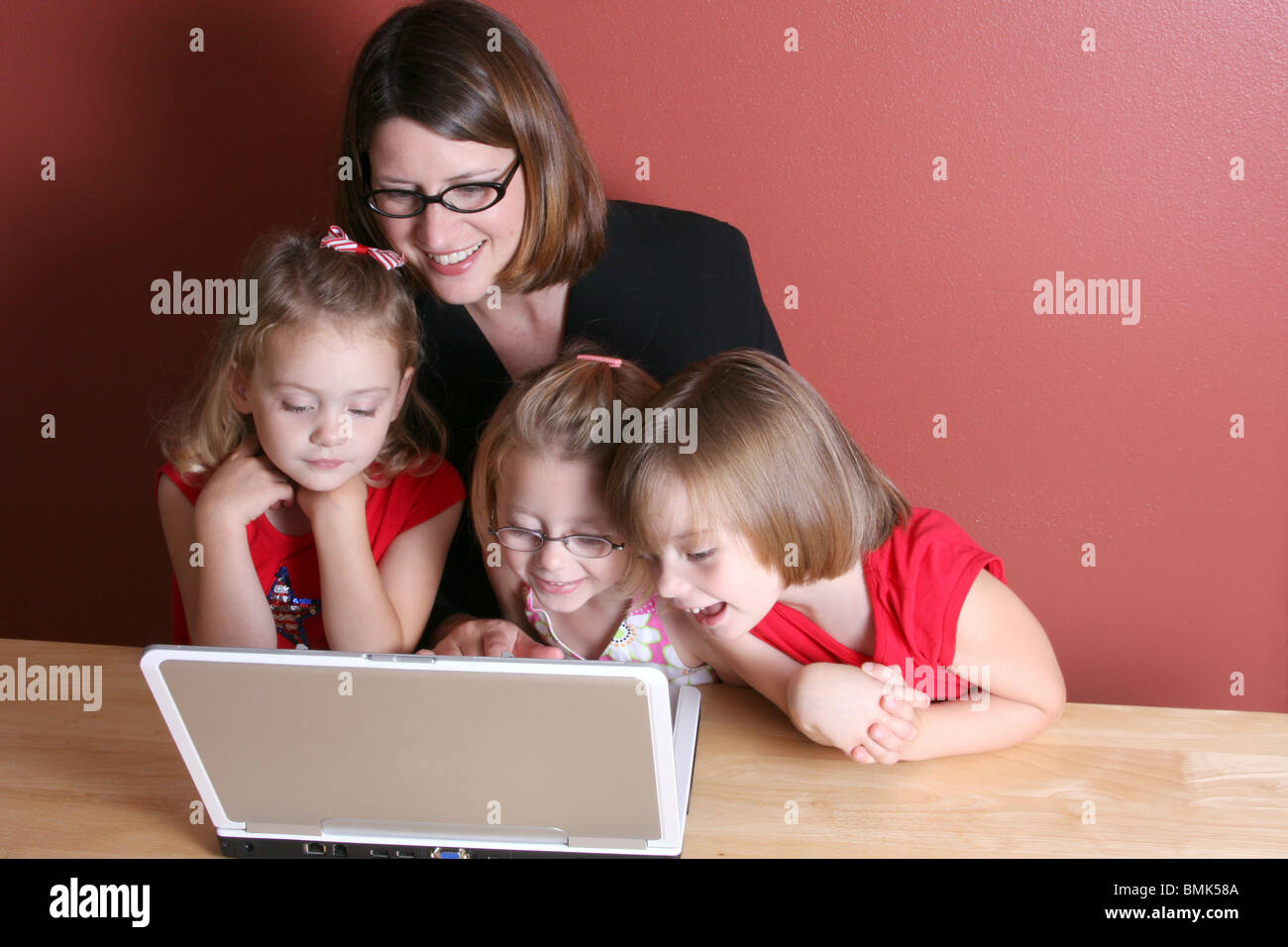 Mom and three girls looking at a laptop computer Stock Photo - Alamy