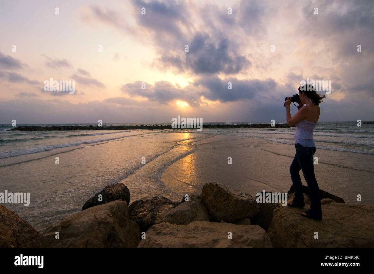 A woman take a photo at sunset in Frishman beach at the Mediterranean ...