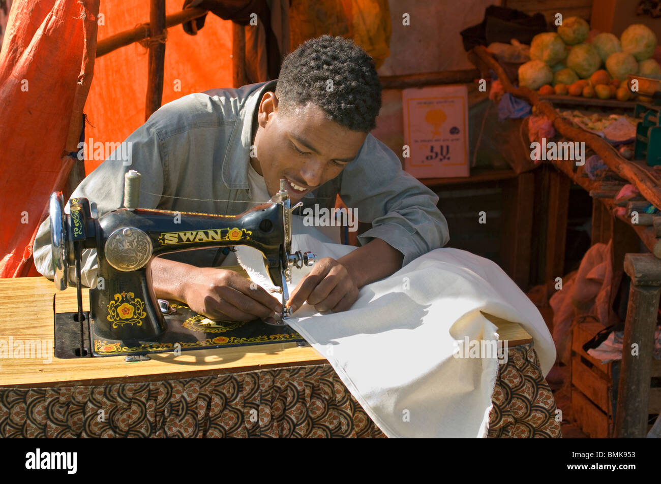 Young male taylor working with old black sewing machine in his orange ...