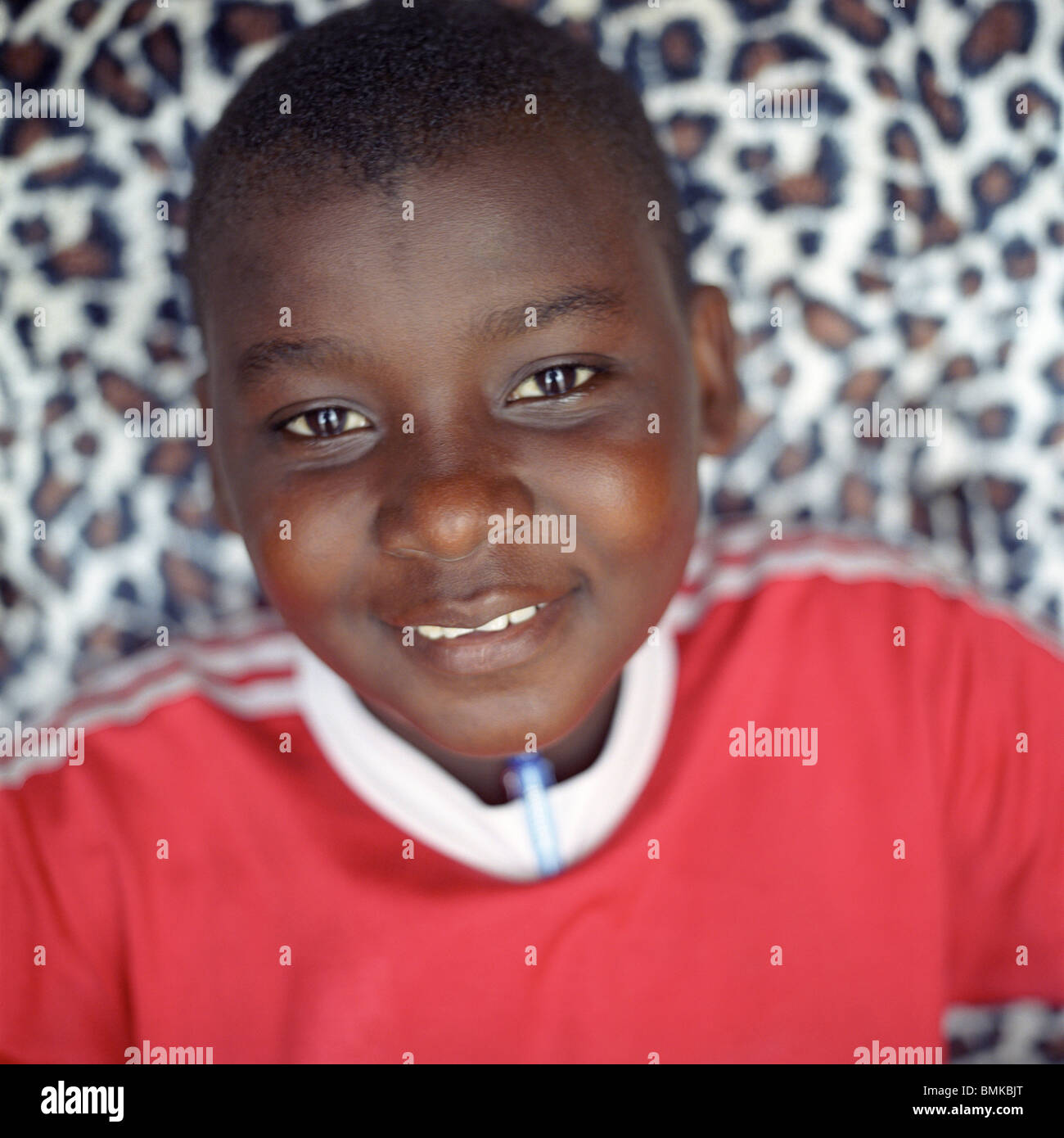 Teenaged african boy in kenya wearing a red shirt looks into the camera ...