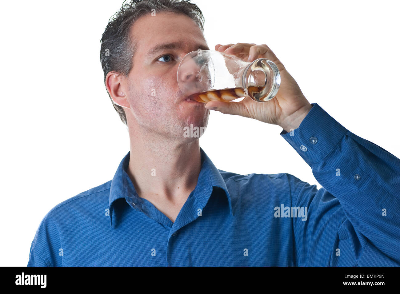 A man in a blue dress shirt, drinking pop from a glass with ice ...