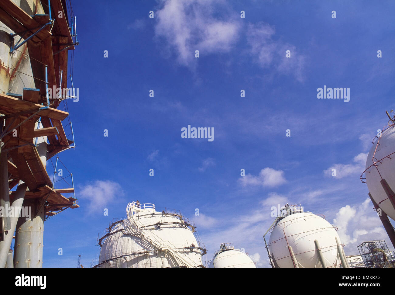 Oil refinery workers standing on scaffold of spherical storage tanks ...