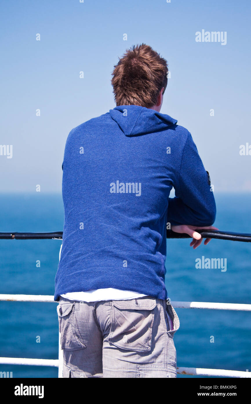 Rear view of a young man leaning on the railing of a ferry or cruise ...