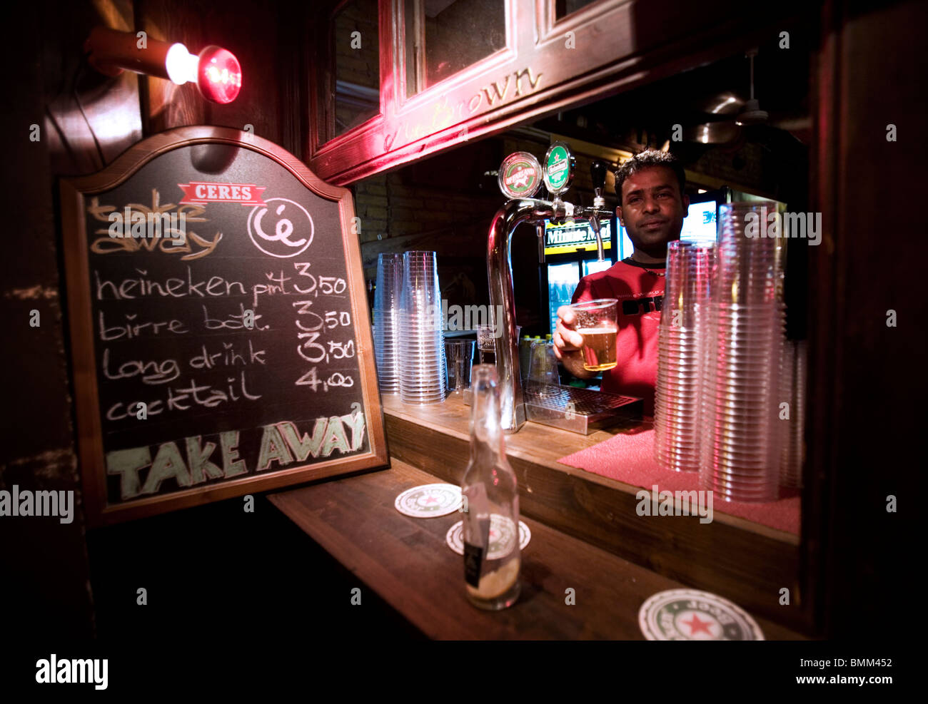 A bartender offers a beer through a bar window at night, with Bar signs ...