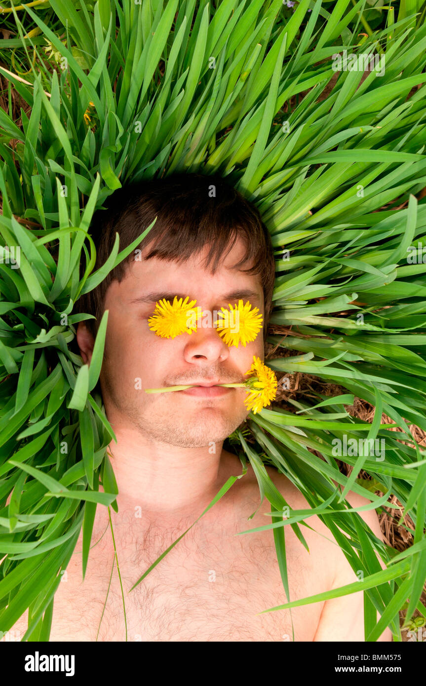 Young man lying on the grass with dandelion flowers on his eyes and in ...