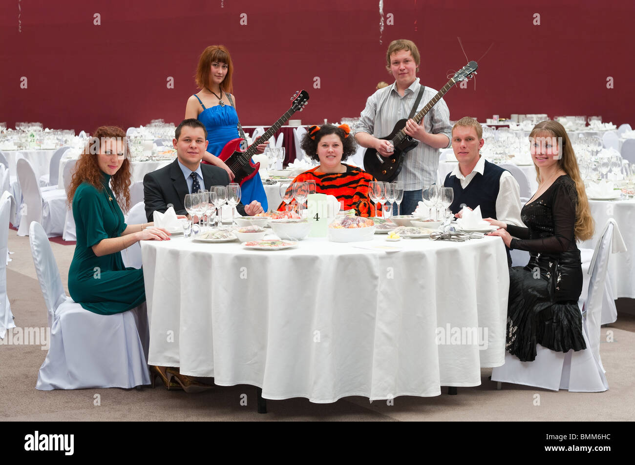 Five young people at round white table in restaurant and two artists ...
