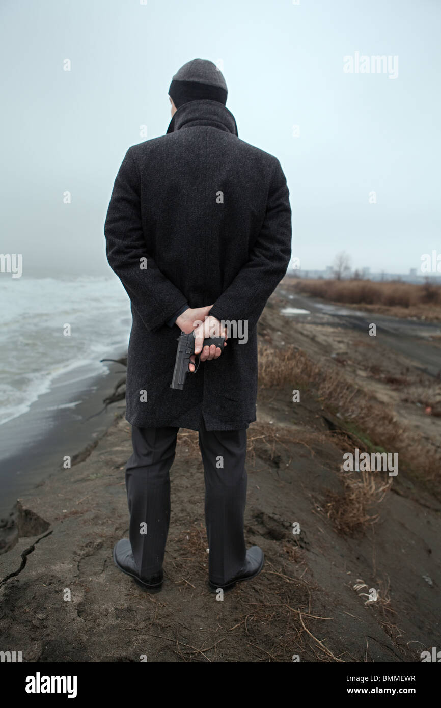 Man holding a loaded gun behind his back Stock Photo - Alamy