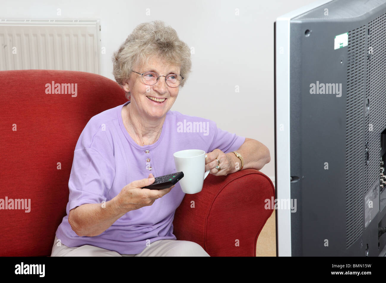 Mature woman sitting holding a tv remote control watching television at ...