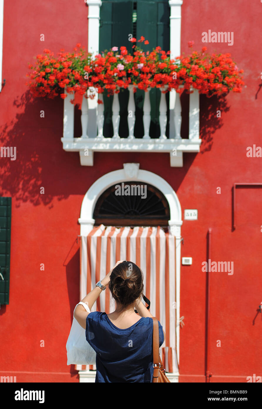 A tourist takes a photo of a bright red house on the island of Burano ...
