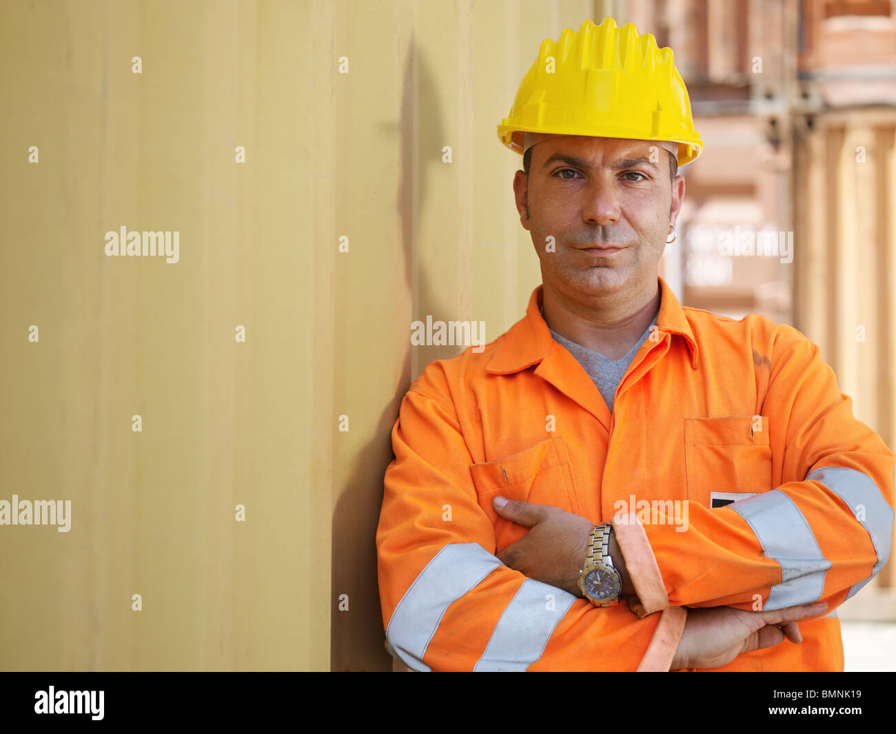 portrait of mid adult worker leaning on cargo container and looking at ...
