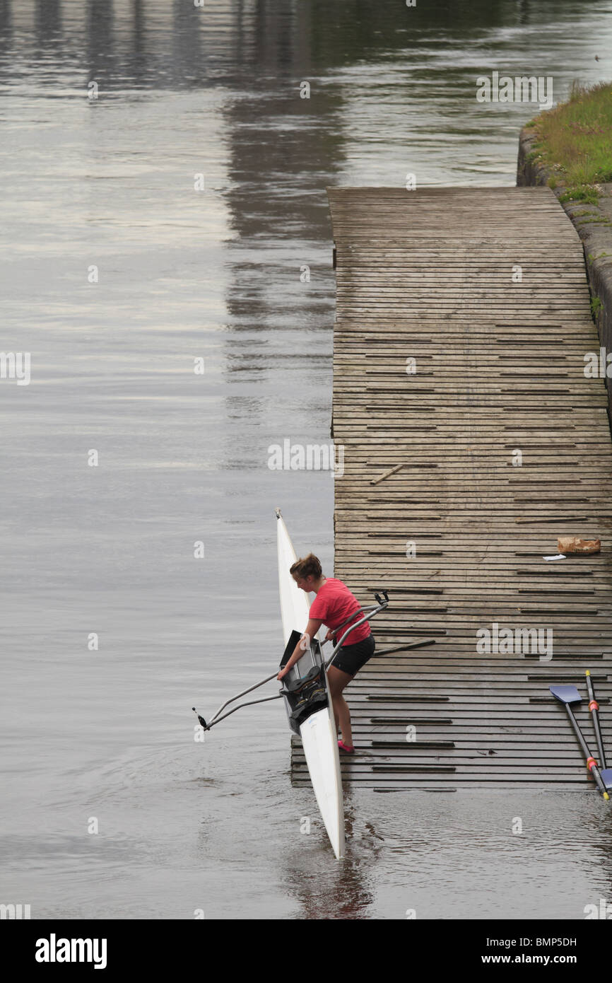 A girl struggles to lift a single scull rowing boat out of the river in ...