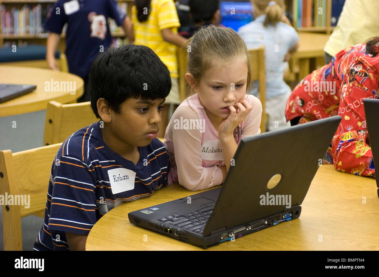 Indian boy and Anglo girl look at laptop computer in elementary school ...