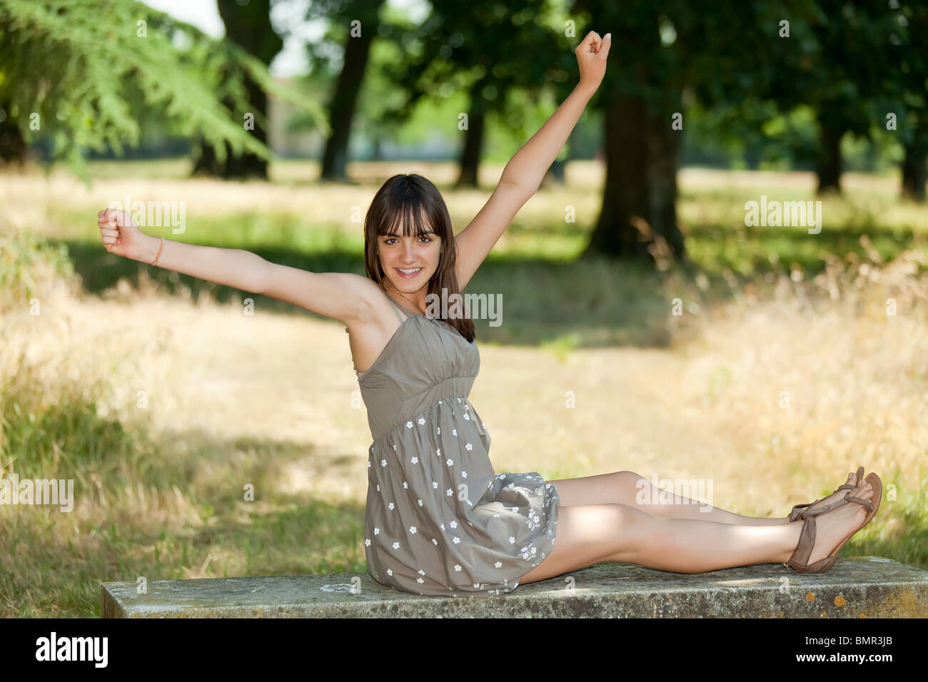 happy teenage girl sitting on park bench and raising arms Stock Photo ...