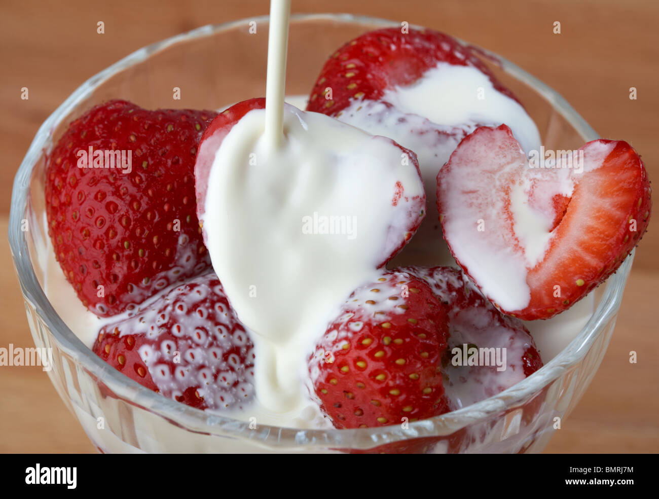 pouring real fresh cream over a bowl of fresh strawberries and cream in ...