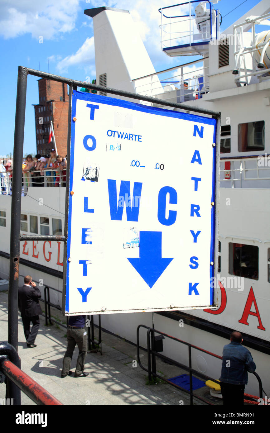 signpost to public restroom entry at waterfront with tour boat in ...