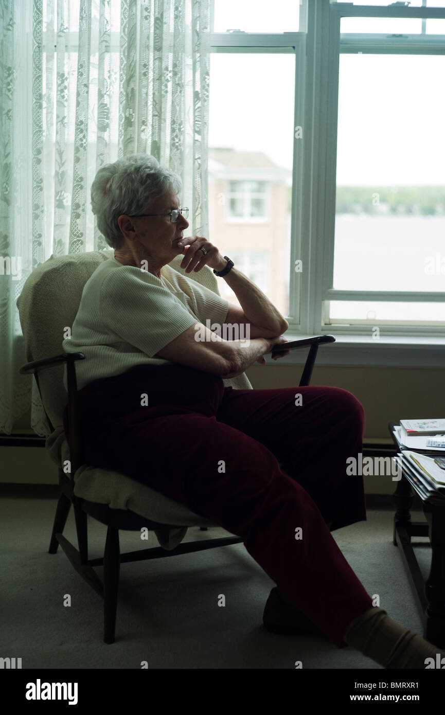 Old woman in profile, sitting in chair looking out window at ocean ...