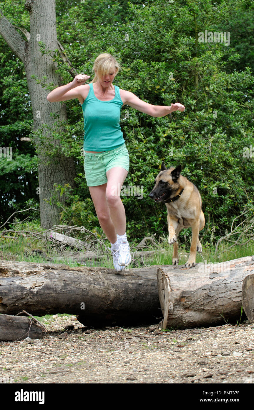 Woman keeping fit running and jumping over logs with a Belgian Shepherd ...