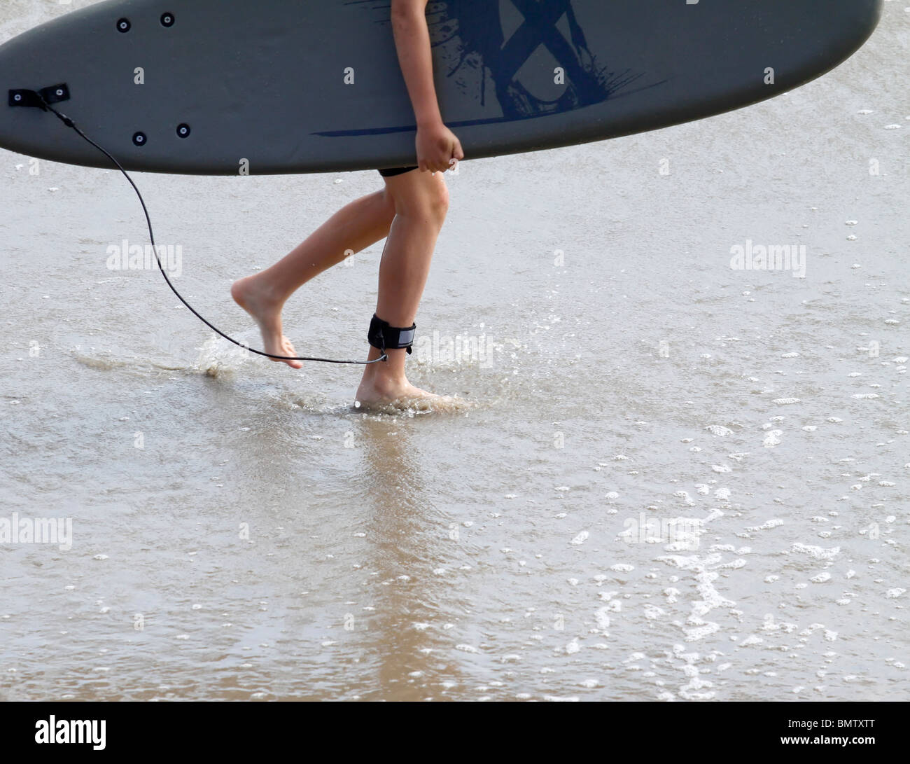 Surfer walking on the beach with a surfboard attached to leg Stock ...