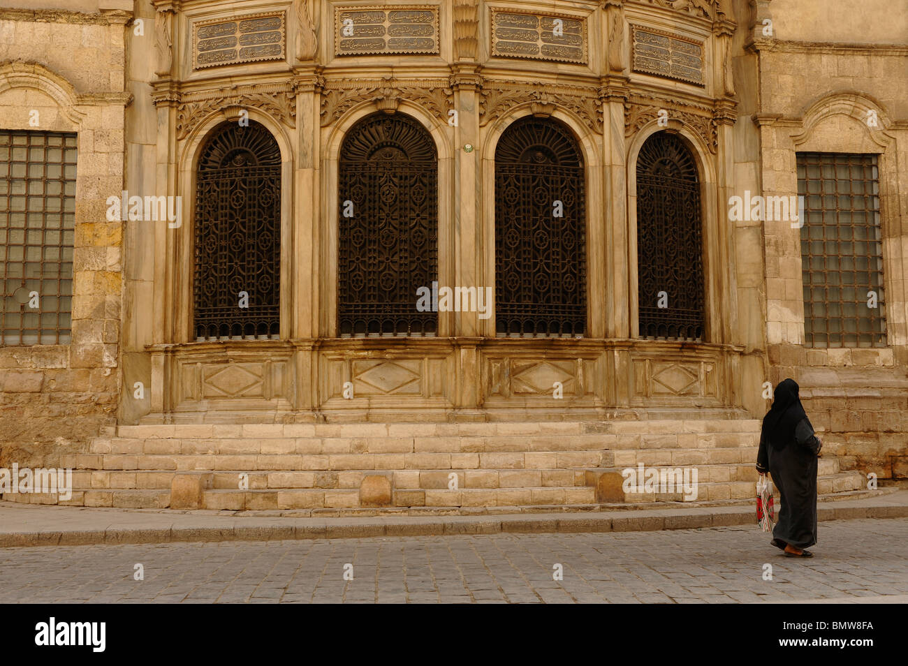muslim lady walking past one of the many mosques in islamic cairo ...