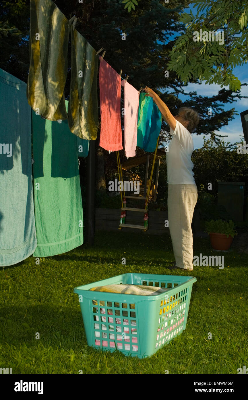 Woman taking dry washing off clothes line and folding it into a plastic ...