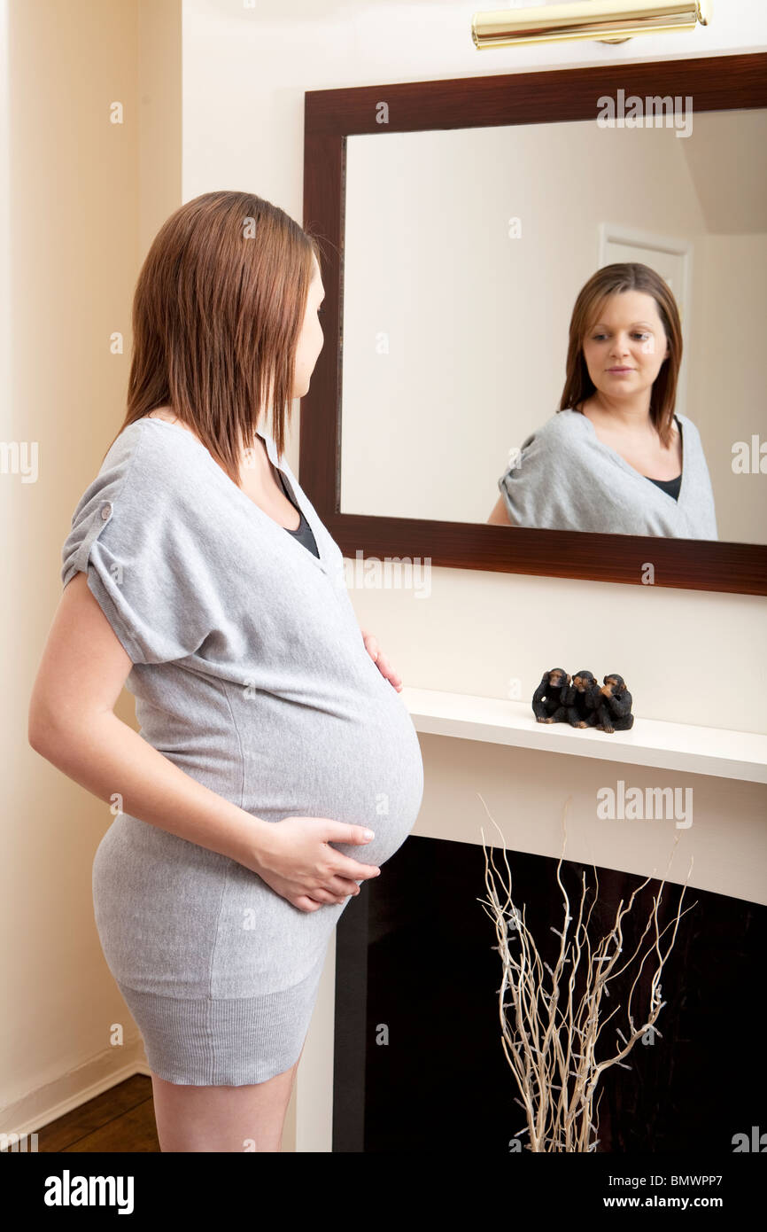 Young pregnant woman looking in the mirror Stock Photo - Alamy