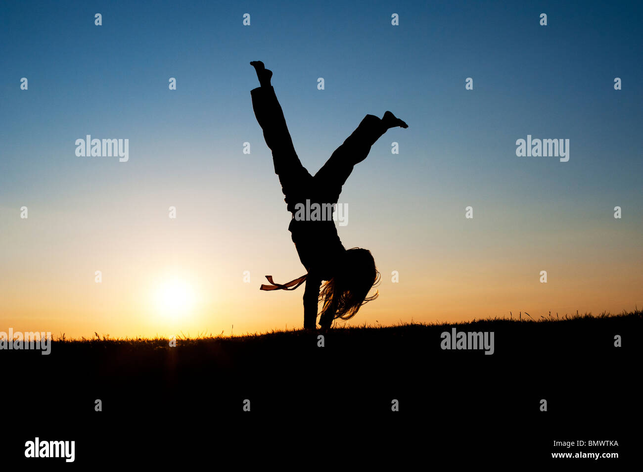 Young Girl energetically having fun doing a handstand at sunset ...