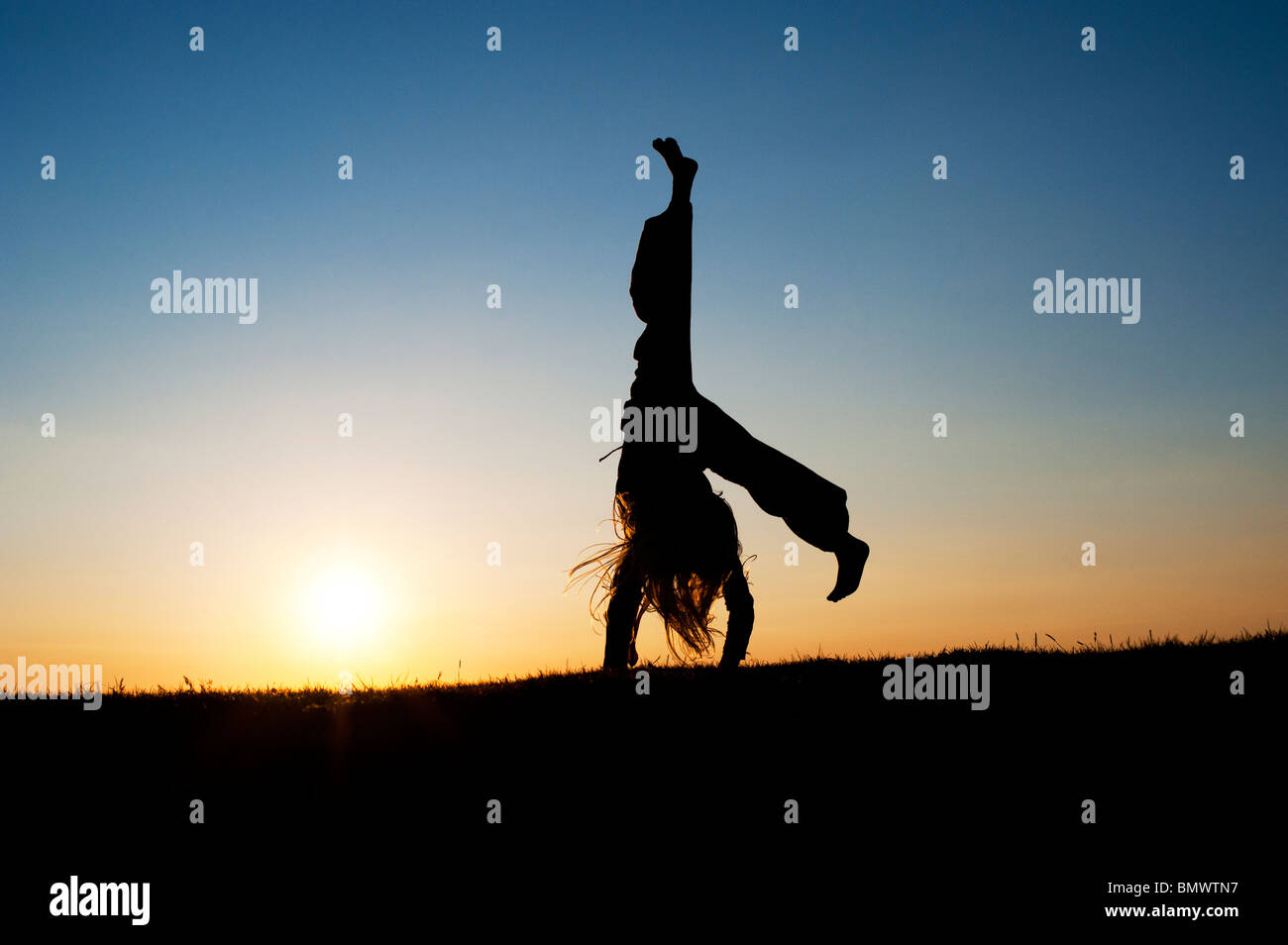Young Girl energetically having fun doing a handstand at sunset ...
