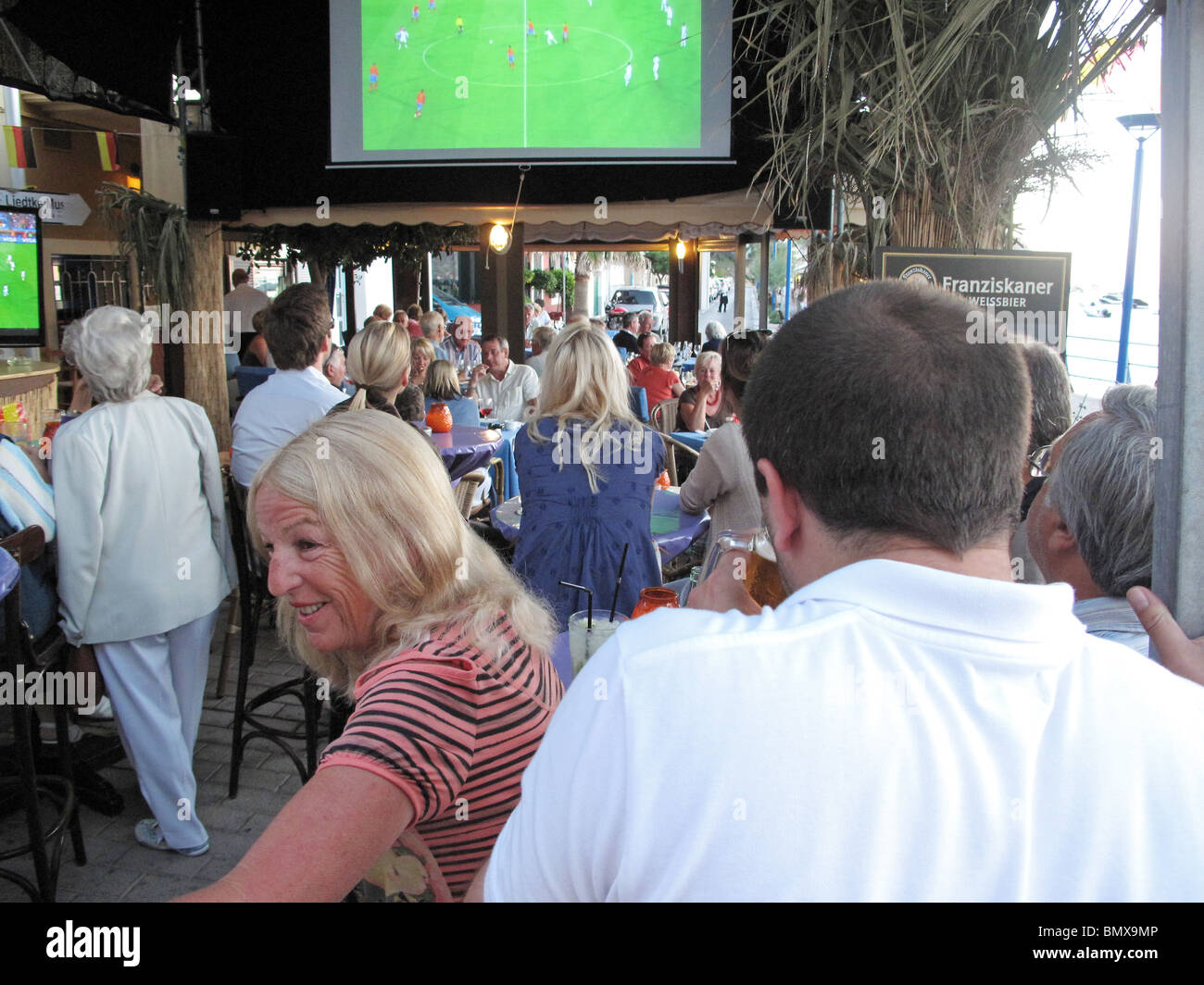 A crowd of people watching The World Cup on an outdoor TV screen at a ...
