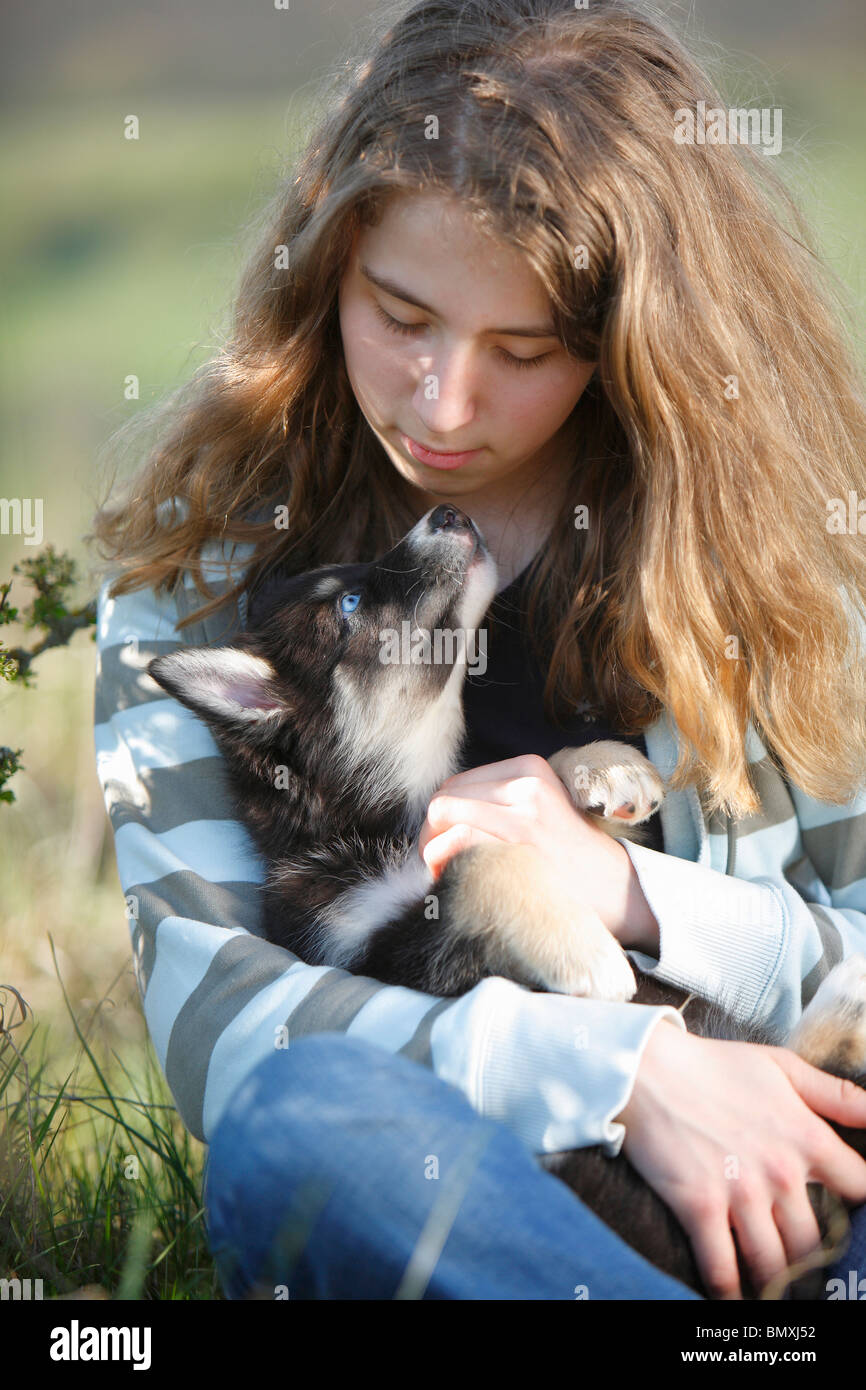 domestic dog (Canis lupus f. familiaris), girl sitting in a meadow ...