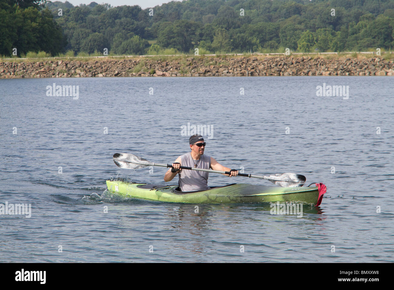 A man male paddling a green kayak. He has sunglasses on he is smiling ...