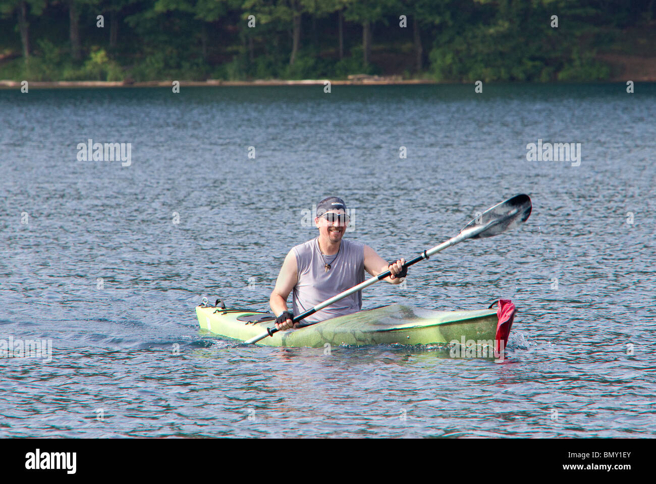 A man male paddling a green kayak. He has sunglasses on he is smiling ...