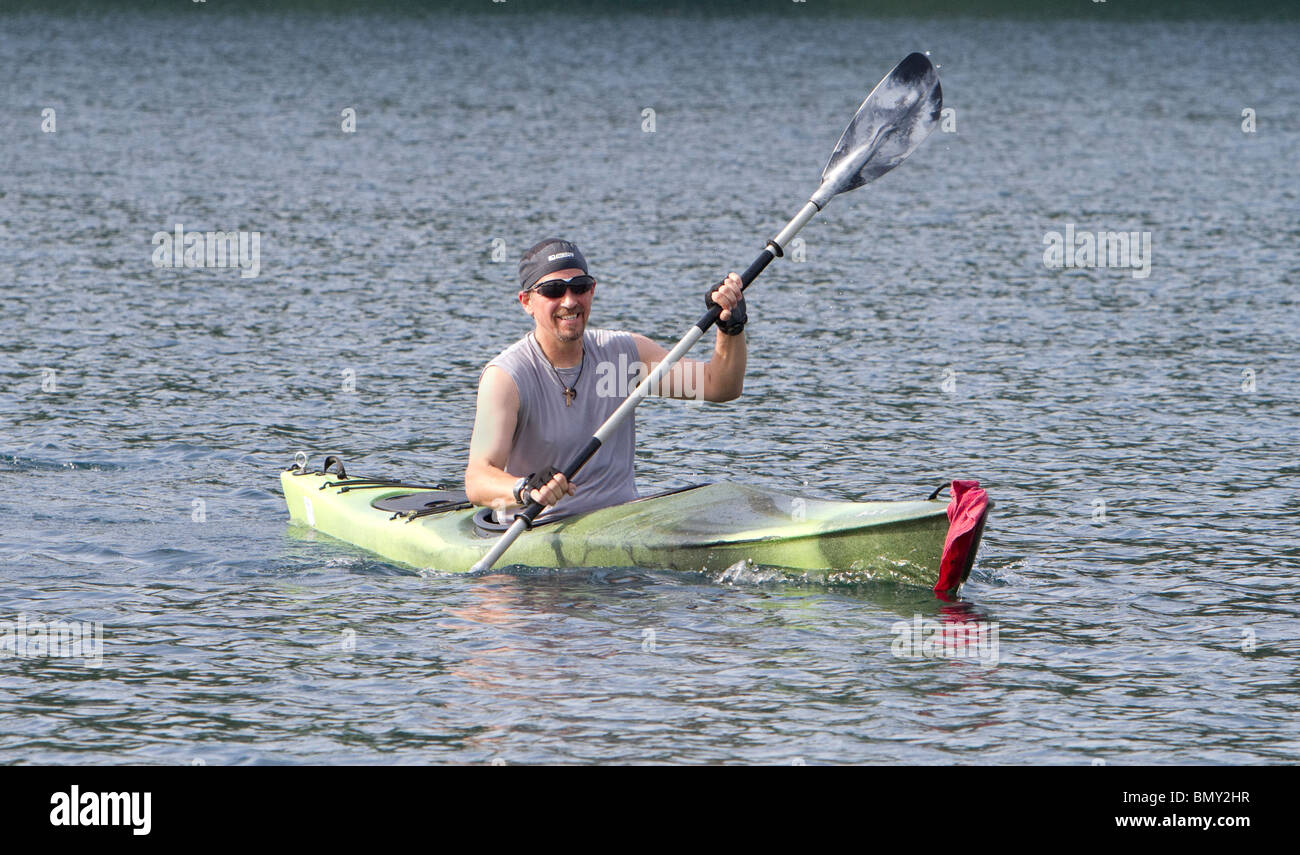 A man male paddling a green kayak. He has sunglasses on he is smiling ...
