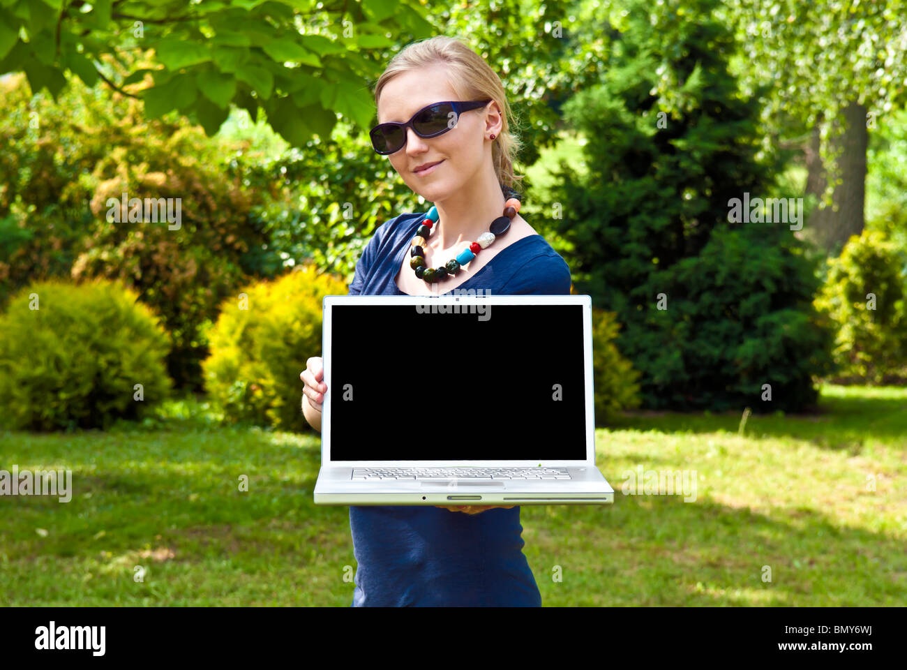 Young blonde woman with computer in the garden.Giving computer, giving ...