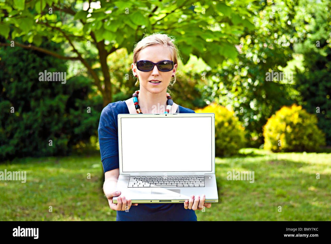 Young blonde woman with computer in the garden.Giving computer, giving ...