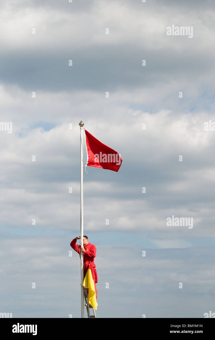 A lifeguard hoisting a safety swimming red flag at Littlehampton in ...