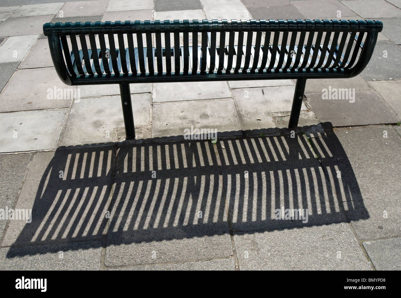 metal public bench with shadow cast in strong sunshine, in whitton ...