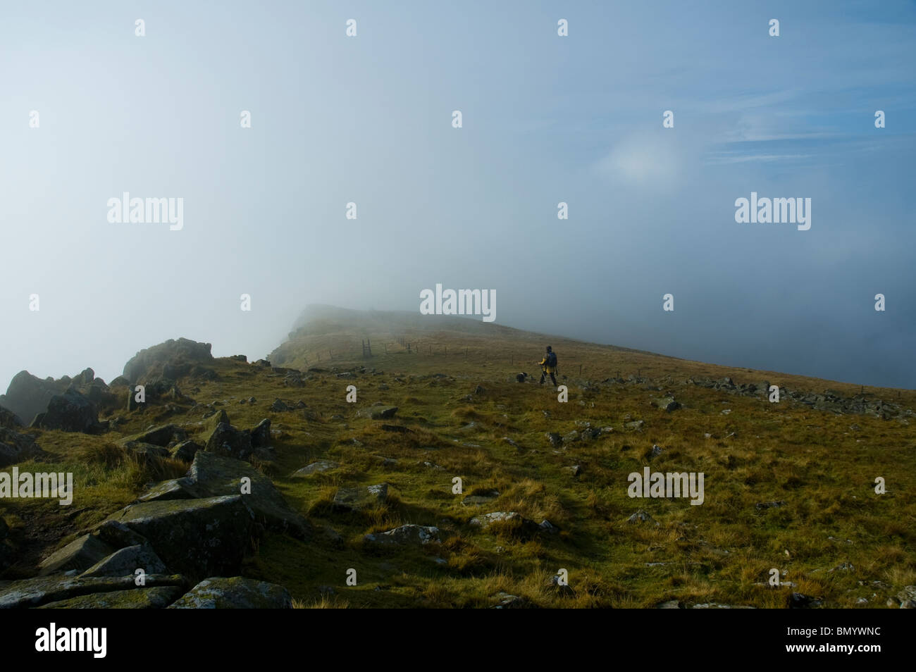 A walker appears through mist and low cloud on the summit of Cadair ...