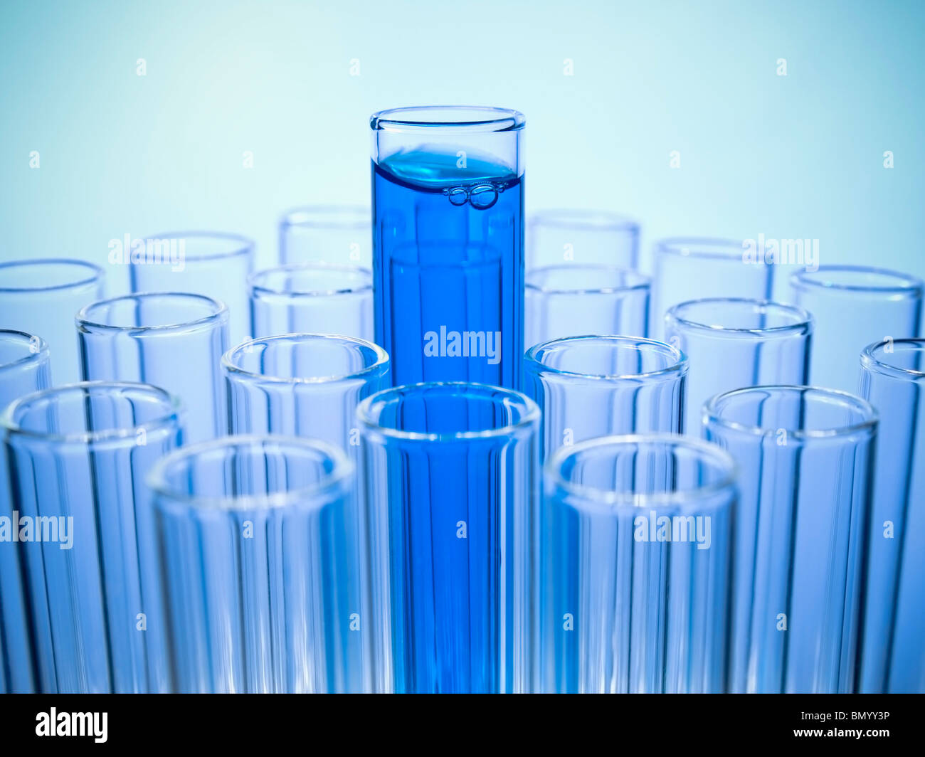 A test tube filled with blue liquid coming out of many empty test tubes ...