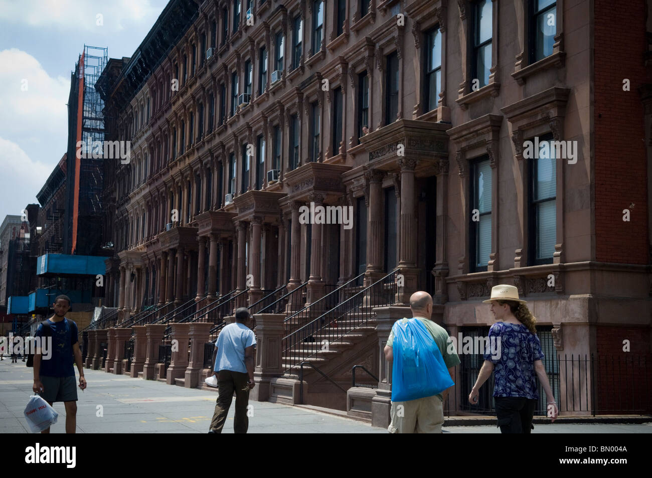 Pedestrians walk down a brownstone block in the Harlem neighborhood of ...