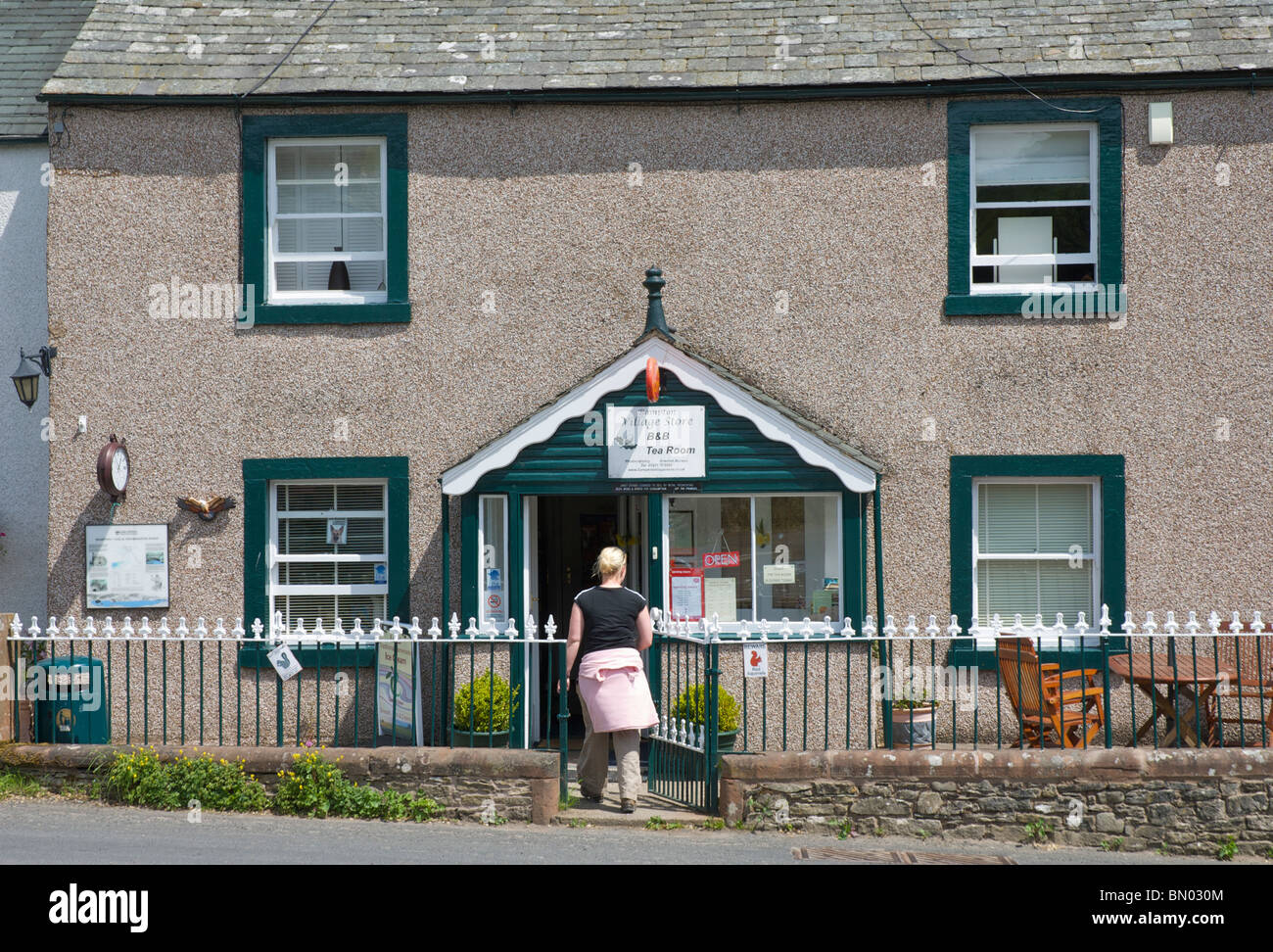 Woman entering shop and Post Office in the village of Bampton, Cumbria ...