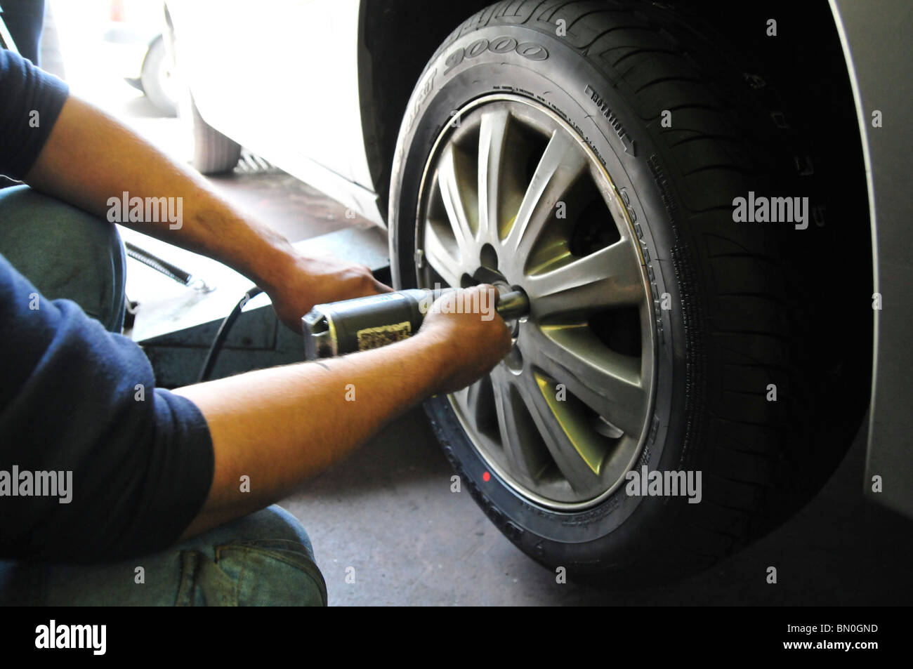 Mechanic uses pneumatic tool to secure the wheel on to the vehicle ...