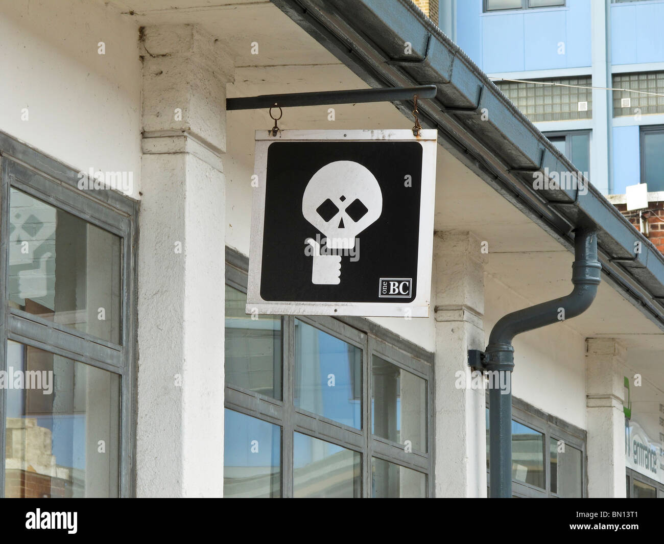 A projecting shop store sign depicting a stylised skull with thumbs up ...