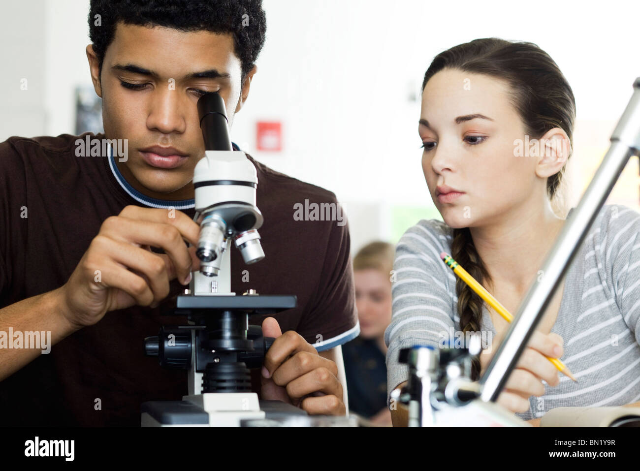 Student looking through microscope in science class Stock Photo - Alamy